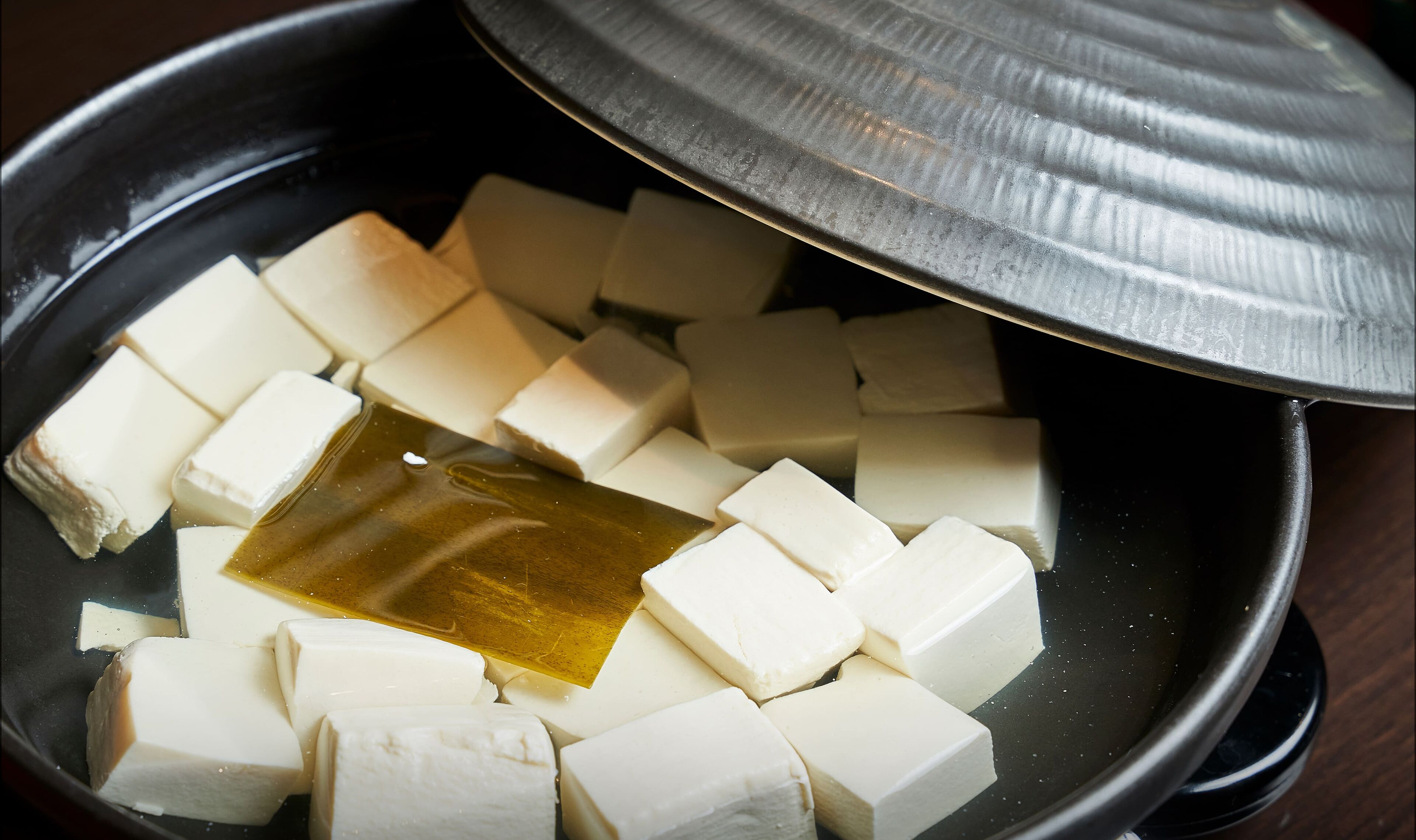 Cubos de tofu numa frigideira com tampa.