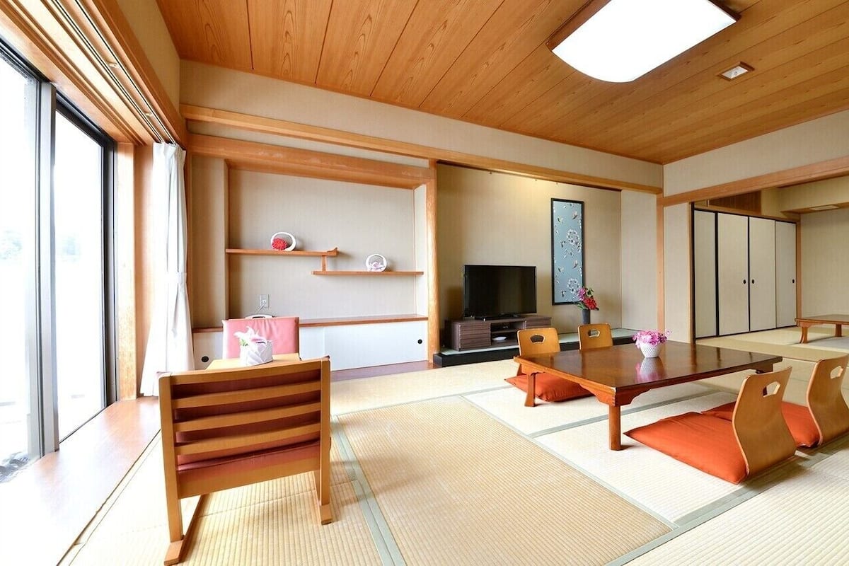 Um quarto em estilo japonês tradicional, com tatames, uma mesa baixa com almofadas, televisão e portas deslizantes.
