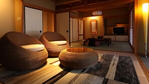 Um quarto japonês tradicional com tatames, duas cadeiras de vime trançada, uma mesa baixa e portas deslizantes.