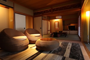 Um quarto japonês tradicional com tatames, duas cadeiras de vime trançada, uma mesa baixa e portas deslizantes.