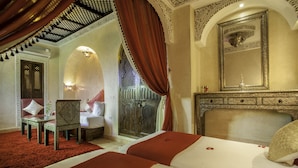 Quarto tradicional com duas camas, um espaço de estar e um espelho decorativo.