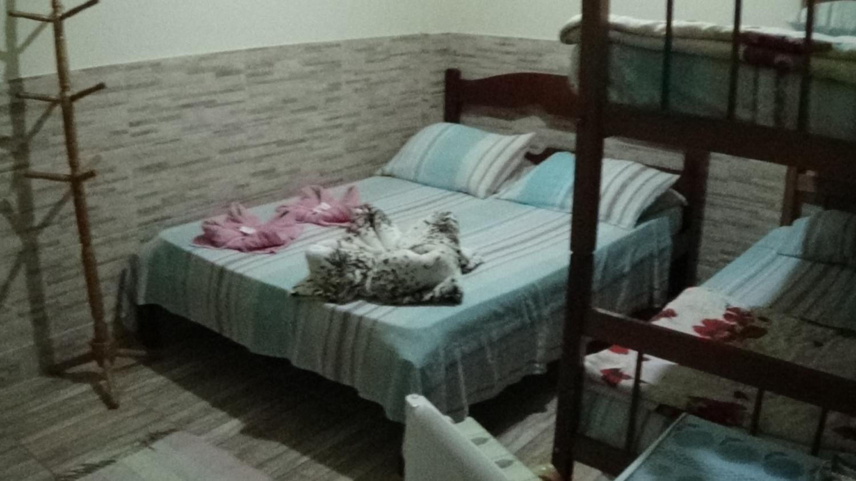 Quarto pequeno com uma cama de solteiro, cabeceira de madeira, colcha listrada e almofada estampada com motivos florais.