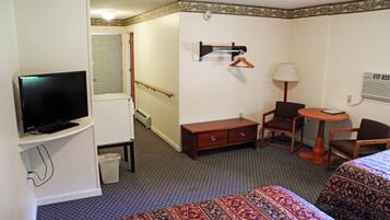 Quarto de hotel com cama, escrivaninha, cadeira, televisão, luminária e cabideiro.