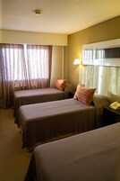 Quarto de hotel com duas camas, uma mesa de cabeceira com telefone e uma janela com cortinas.