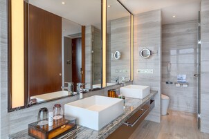 Uma casa de banho moderna com duas grandes pias brancas, uma cabine de duche com portas de vidro e um espelho grande.