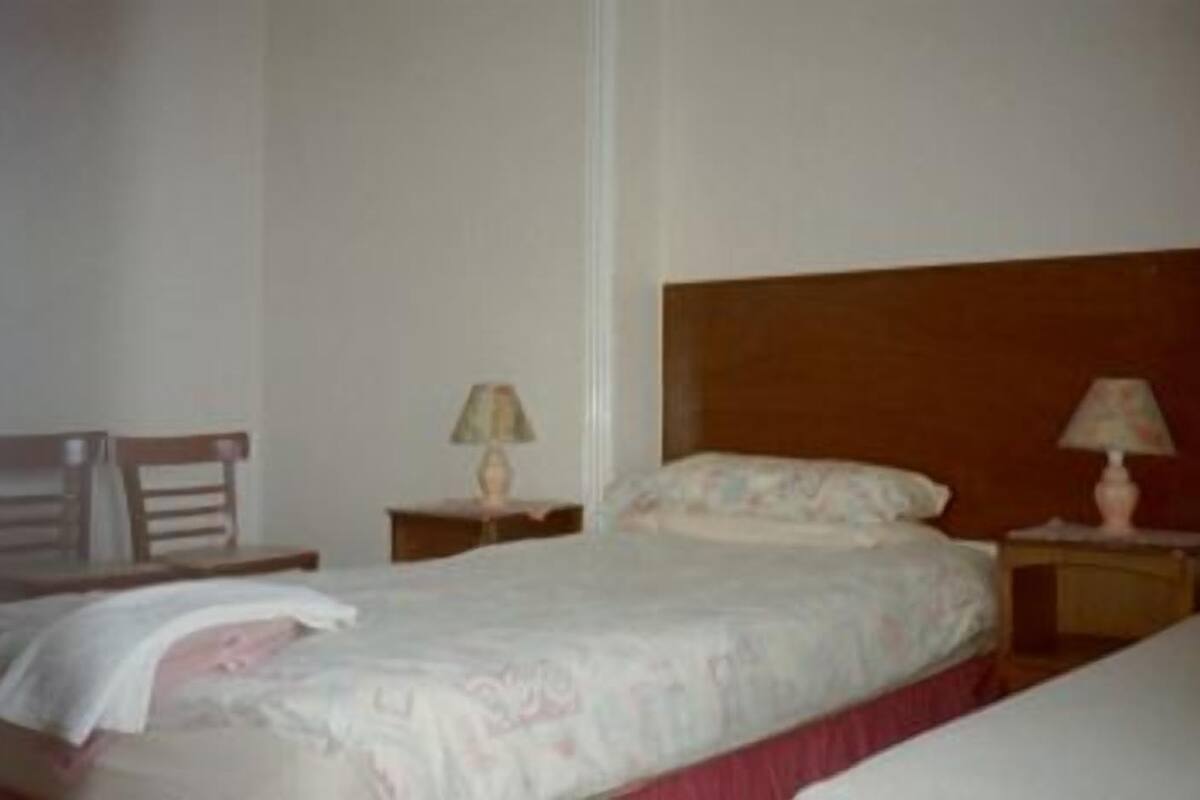 Quarto simples e limpo com uma cama, uma cadeira e duas mesas de cabeceira com luminárias.