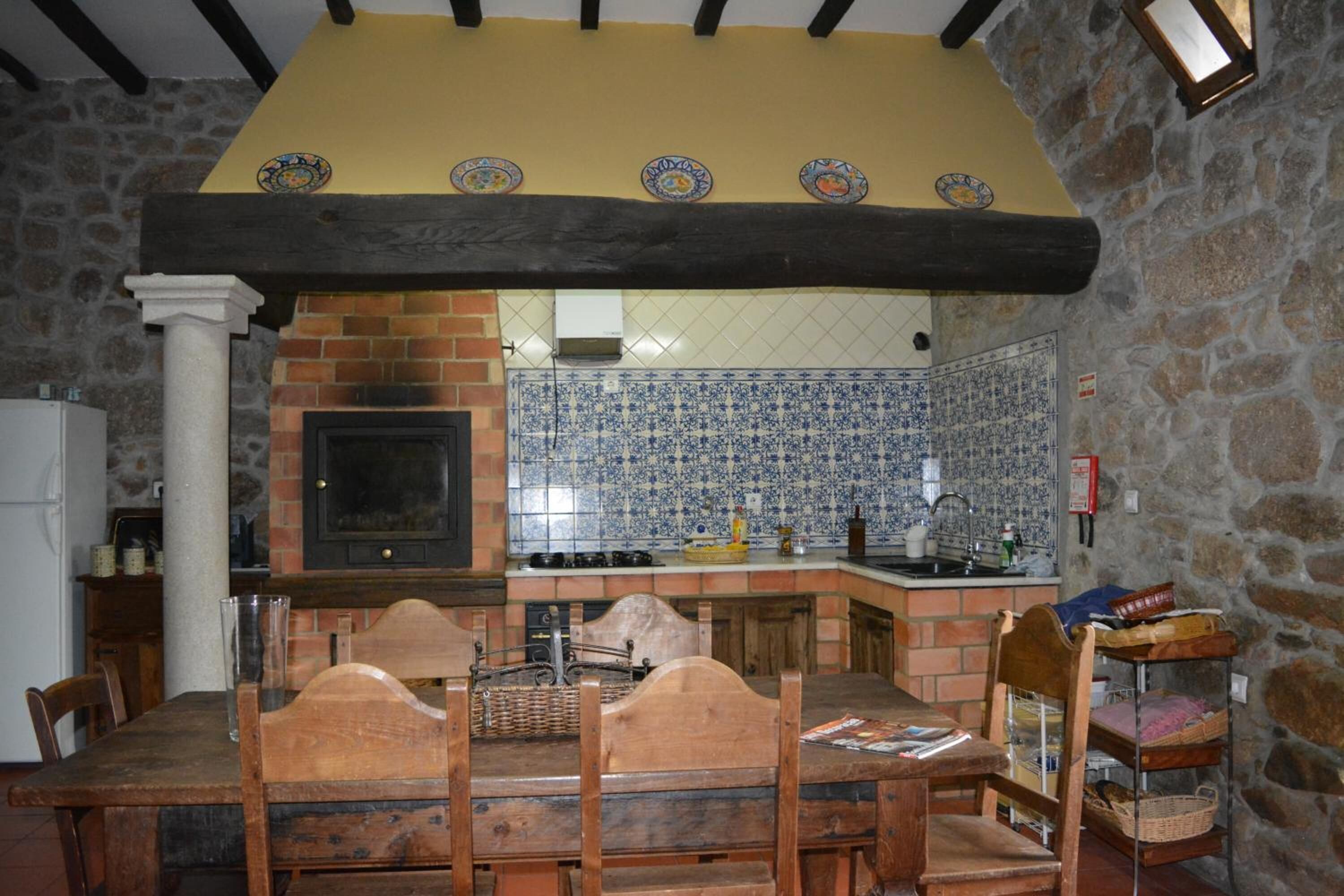 Uma cozinha rústica com lareira de tijolos, cadeiras de madeira e painel de azulejos.