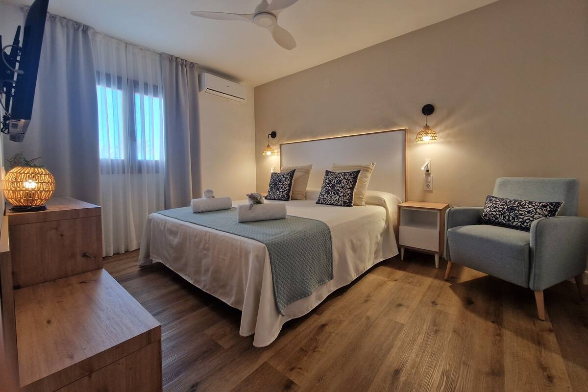 Quarto de hotel moderno com uma cama grande, uma escrivaninha, uma cadeira e um ventilador de teto.