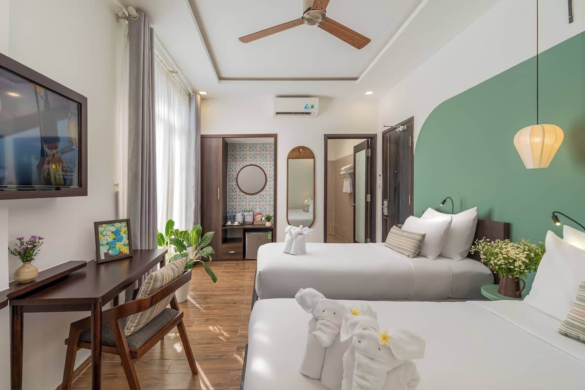 Quarto de hotel com cama, escrivaninha, televisão e ventilador de teto.
