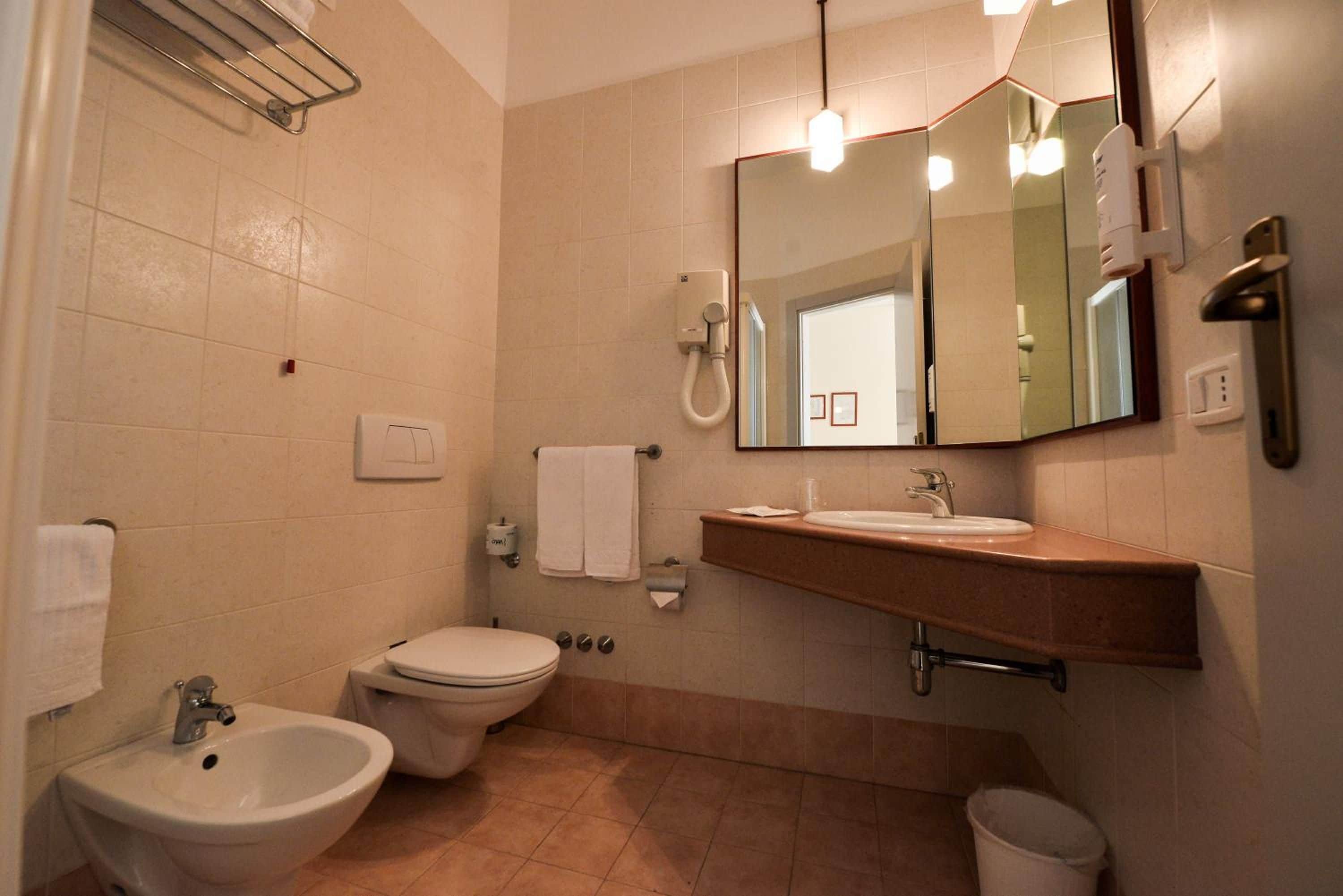 Casa de banho com bidé, sanita, lavatório, espelho e porta-toalhas.