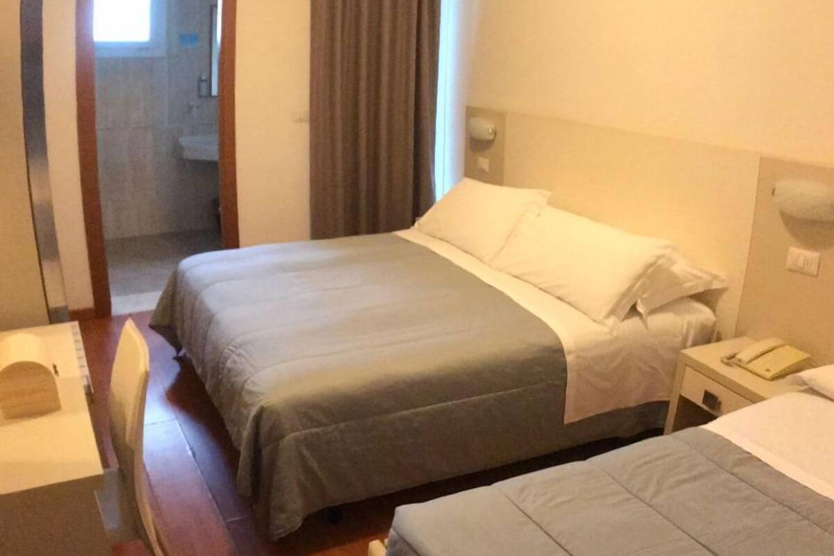 Quarto de hotel com duas camas, uma escrivaninha e uma cadeira.