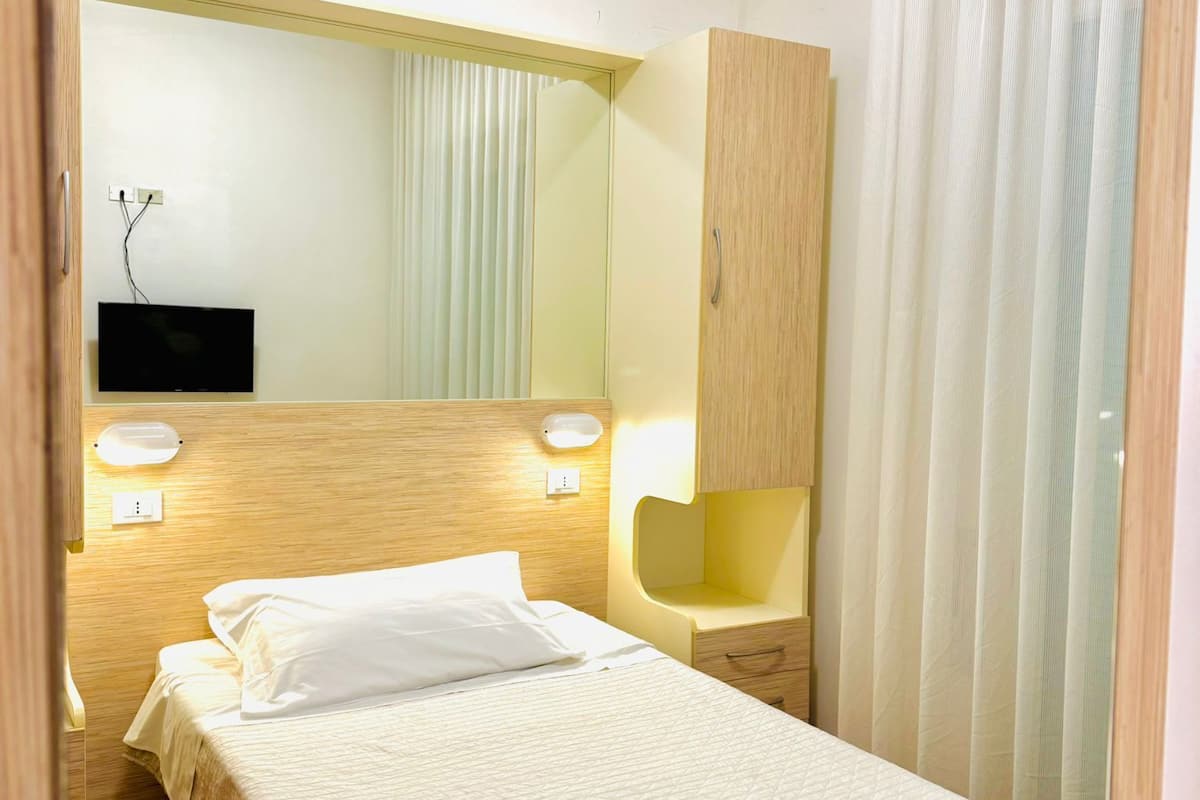 Quarto de hotel com cama, abajures, espelho e armário.