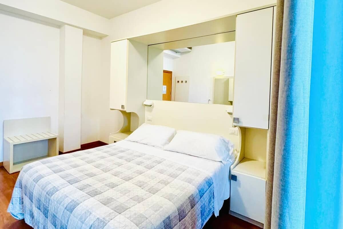 Quarto com cama, mesas de cabeceira, espelho e guarda-roupa.