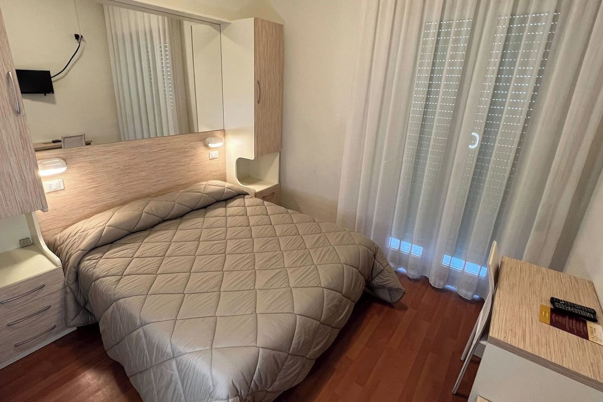 Quarto com cama, mesas de cabeceira, espelho, cortinas e televisão.