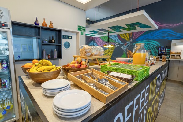 Um balcão de café da manhã com frutas, bebidas e opções para o café.