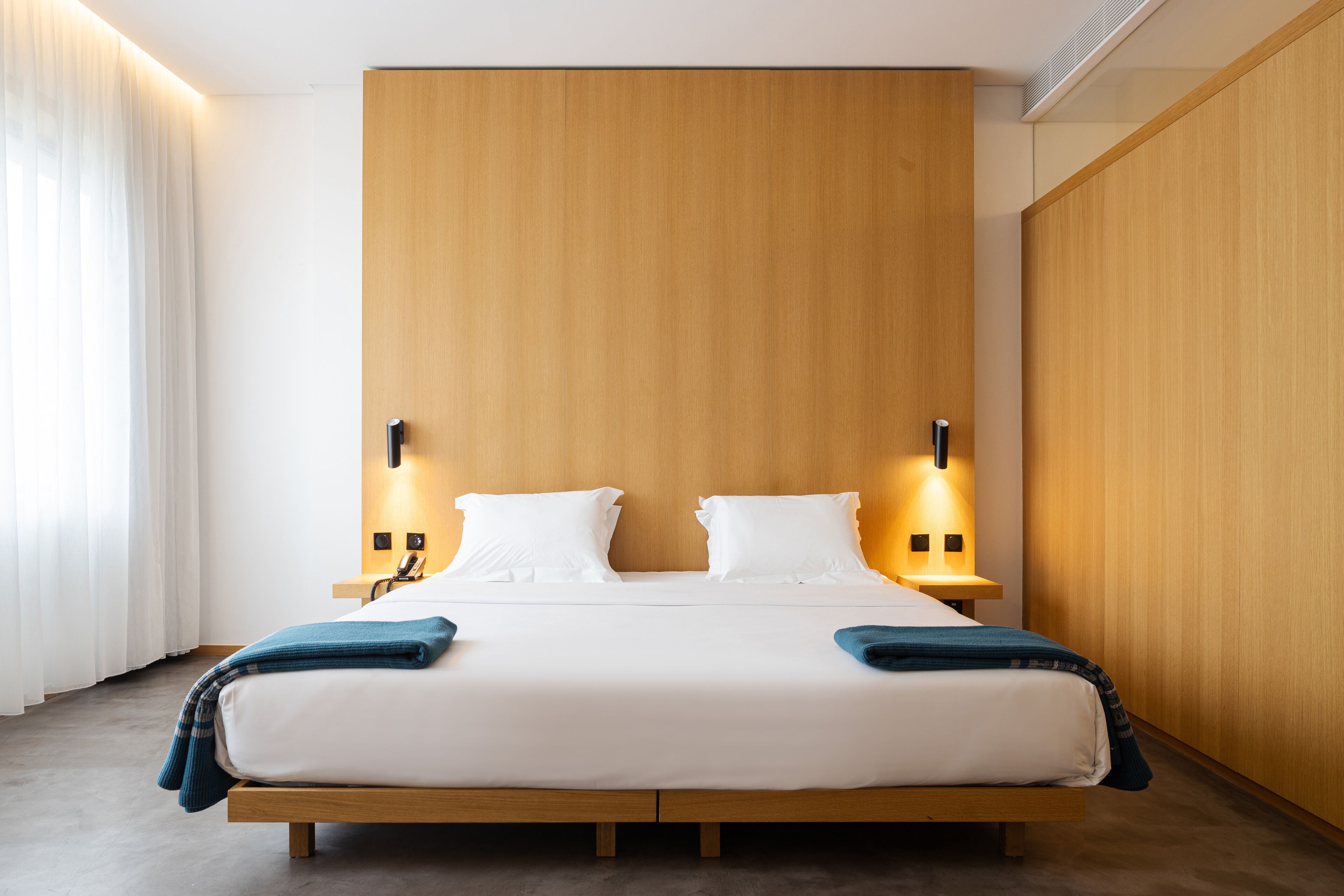 Quarto de hotel moderno com cama grande, cabeceira de madeira e abajures laterais.