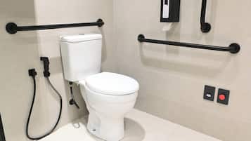 Casa de banho moderna com sanita branca, barras de apoio, chuveiro manual e dispensador de papel higiénico.