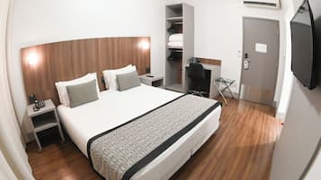 Quarto de hotel com uma cama grande, uma escrivaninha, uma cadeira, um guarda-roupa e uma televisão.