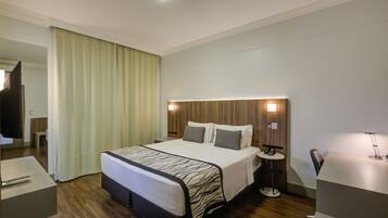 Quarto de hotel com cama, mesa de cabeceira e escrivaninha com abajur.