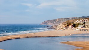 Uma vila costeira com edifícios numa encosta com vista para a praia e o mar.
