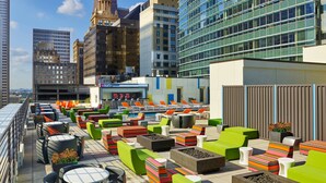 Terraço no telhado com área de estar ao ar livre, piscina e edifícios da cidade ao fundo.