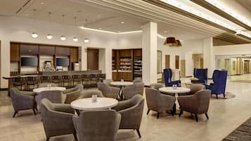 Um hall de hotel moderno com área de bar, assentos e balcão de recepção.