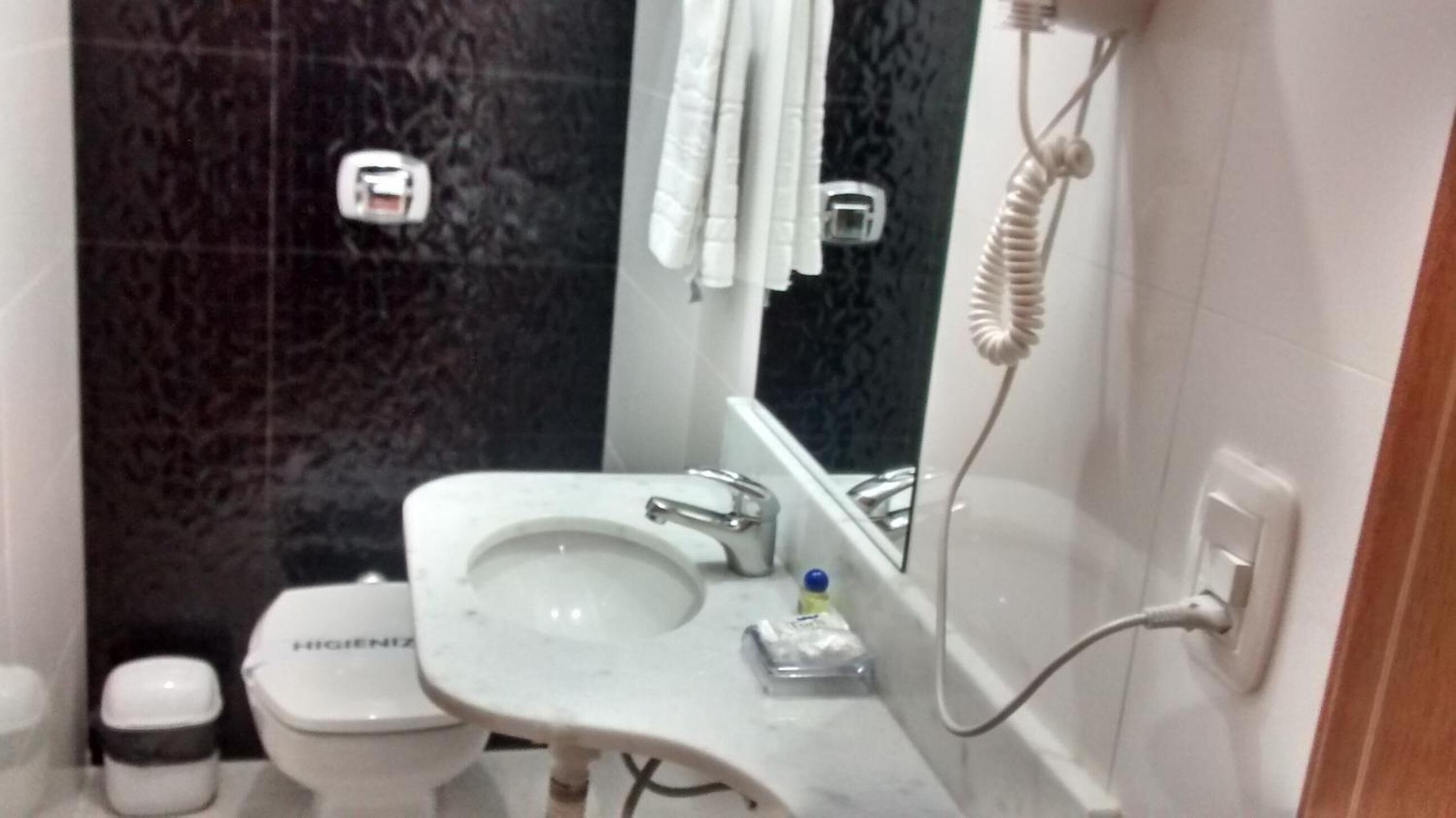 Casa de banho com lavatório branco, espelho, porta-toalhas e sanita.