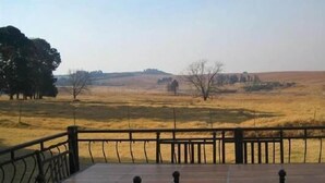 Vista de uma varanda com vista para um campo seco e aberto, com árvores esparsas e colinas ao longe.