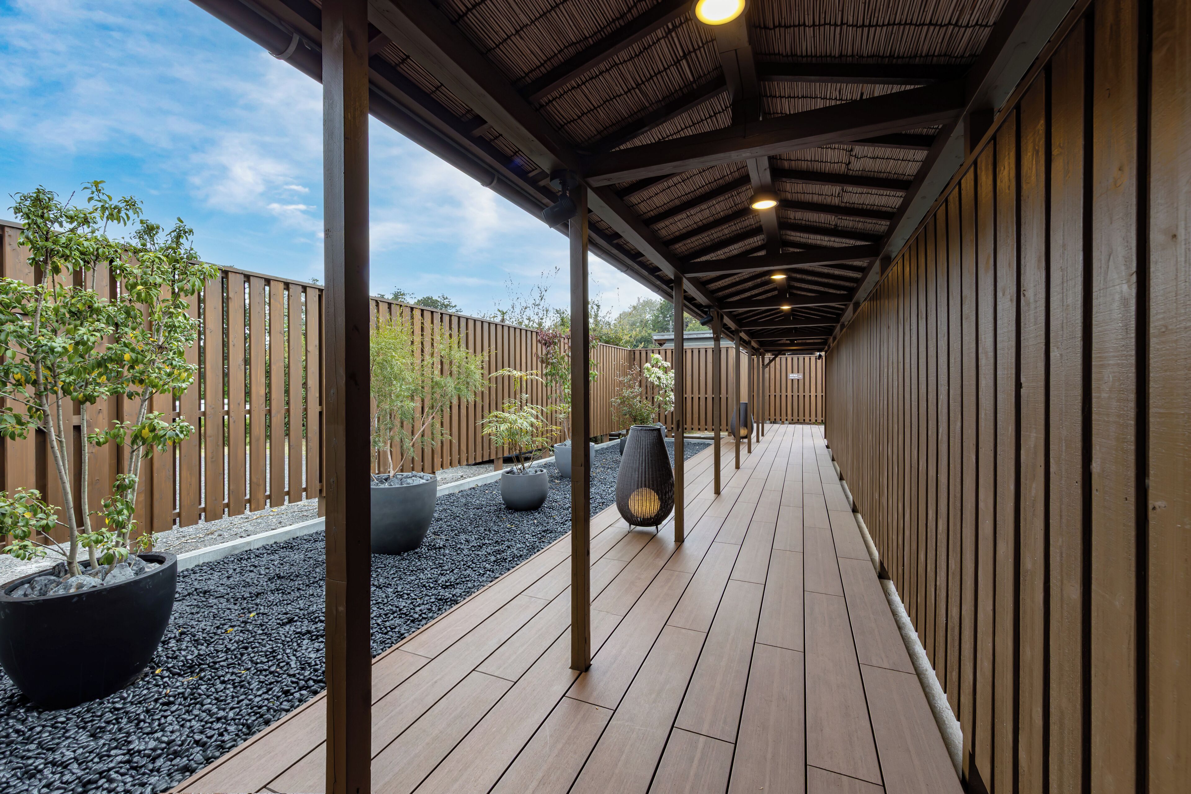 Um espaço ao ar livre coberto com deck de madeira, vasos pretos e cerca de madeira.