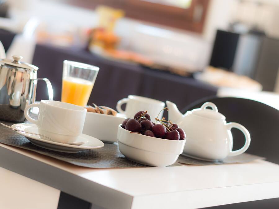 Uma mesa com disposição para café da manhã, incluindo um coador de café, xícara, copo de suco de laranja, tigela de cerejas e uma chaleira.