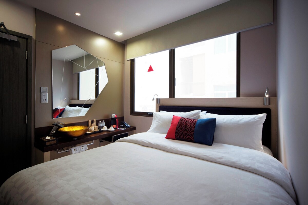 Quarto de hotel moderno com uma cama grande, mesa de cabeceira com cuba, espelho e janela com vista.