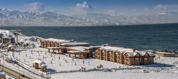 Estância coberta de neve com vários edifícios, uma praia e montanhas ao fundo.