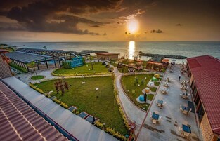 Um hotel à beira-mar com área de pátio, mobiliário de exterior e vista para o oceano ao pôr do sol.