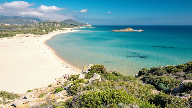Paisagem costeira com praia arenosa, águas turquesa cristalinas e afloramentos rochosos.