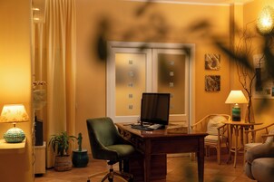Quarto de hotel com escrivaninha, computador, cadeira, luminária e planta em vaso.