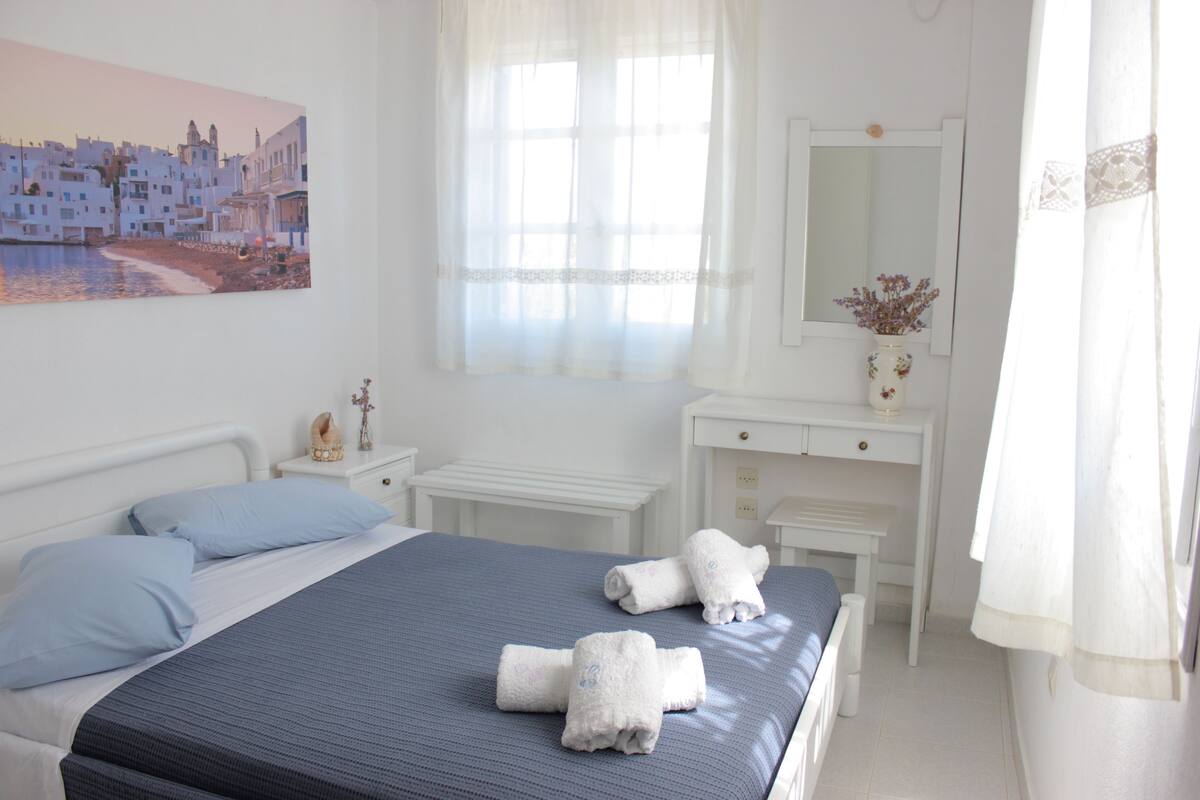 Quarto de hotel com cama, mesa de cabeceira, cômoda, espelho e um quadro na parede.