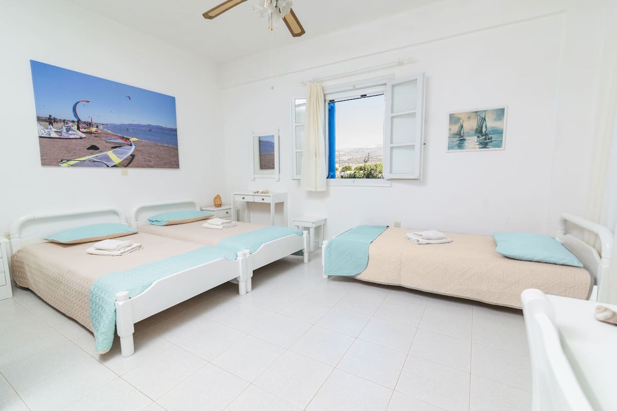 Quarto com duas camas, janela com vista para a praia e um quadro de um veleiro.