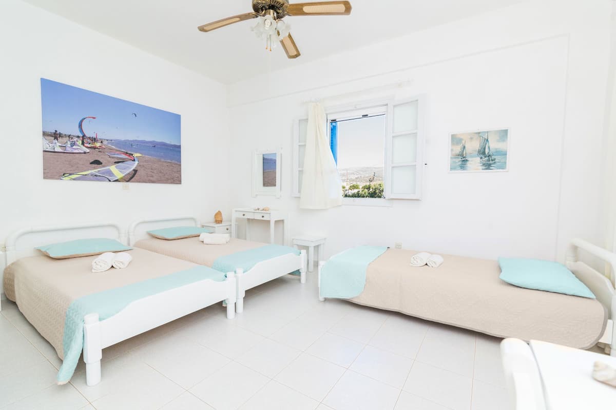 Quarto com três camas, uma escrivaninha e um ventilador de teto.
