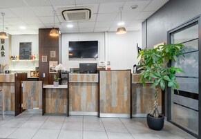 Uma área de recep ção com balcão de madeira, televisão de tela plana, espaço de bar com menu e um vaso de planta.