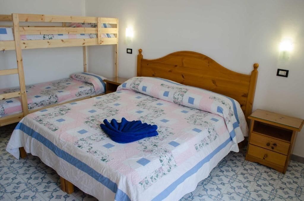 Quarto com duas camas beliche, cabeceira de madeira, mesa de cabeceira e criado-mudo.