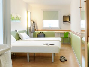 Quarto de hotel com duas camas, uma escrivaninha, uma cadeira, uma mala e uma televisão.