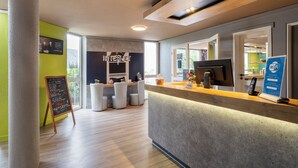 Uma área de recepção moderna, com balcão, assentos e um quadro negro com informações.