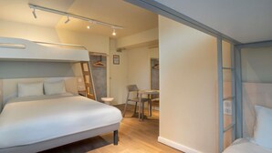 Quarto de hotel moderno com uma cama beliche, uma mesa pequena, uma cadeira e uma escrivaninha.