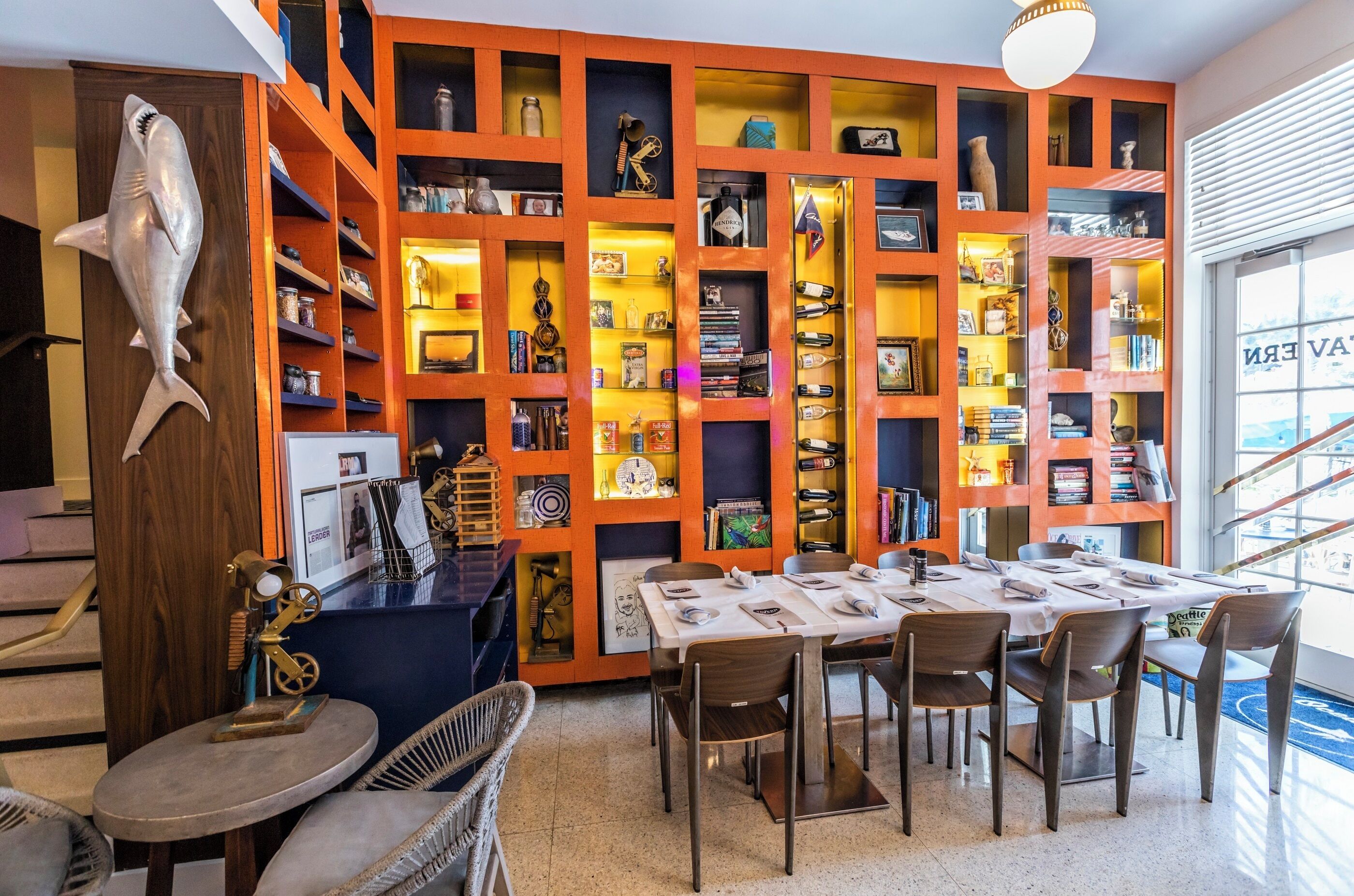 Uma área de refeições com uma mesa posta para quatro pessoas, rodeada por estantes laranjas cheias de diversos objetos.