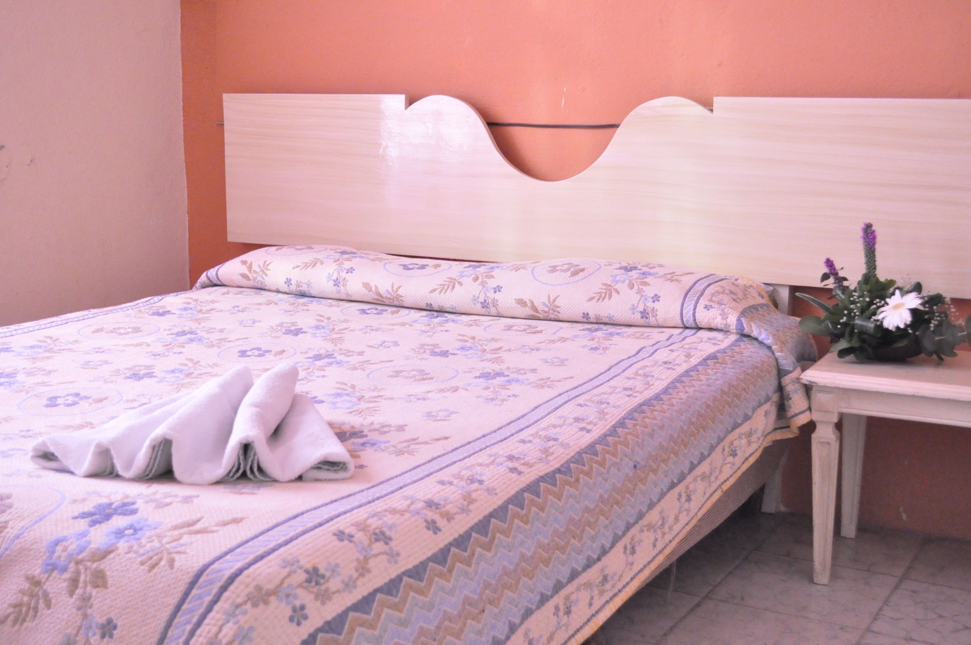 Cama bem arrumada com colcha estampada em flor e toalha dobrada ao lado.