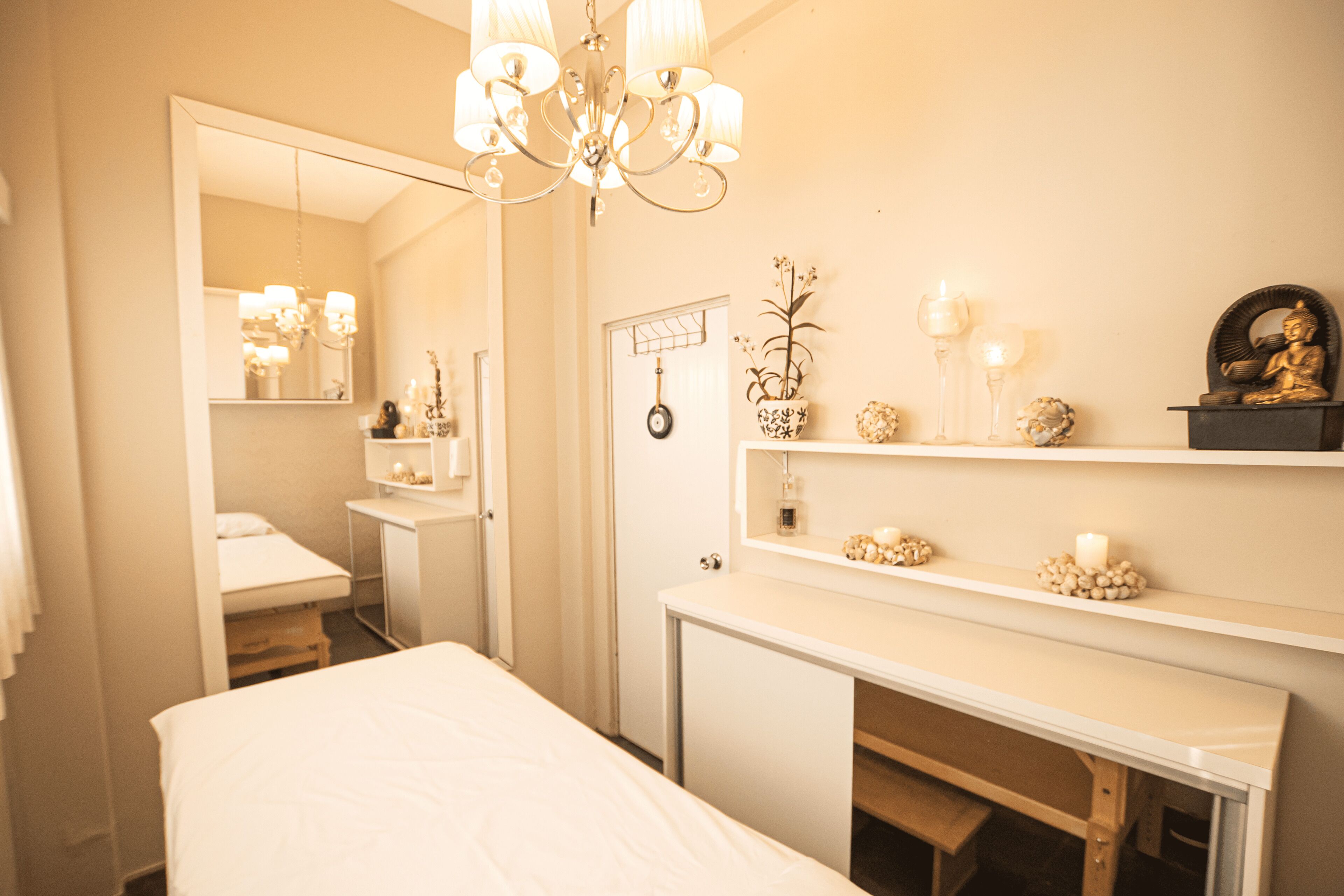 Quarto de hotel com cama, toucador com espelho, candelabro, prateleira com objetos decorativos e uma estátua de Buda.