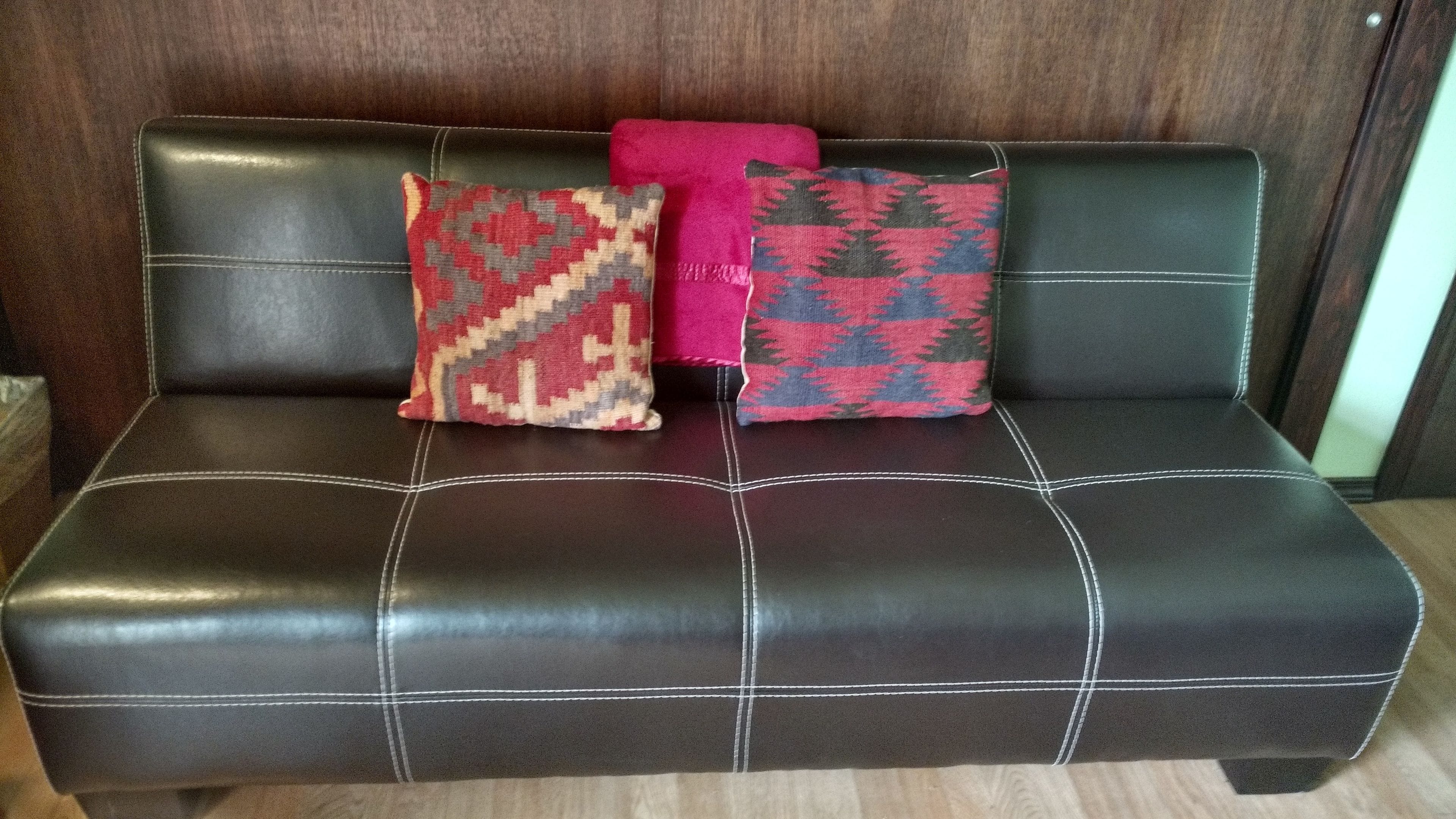 Um sofá de couro preto com costura branca e três almofadas decorativas estampadas.