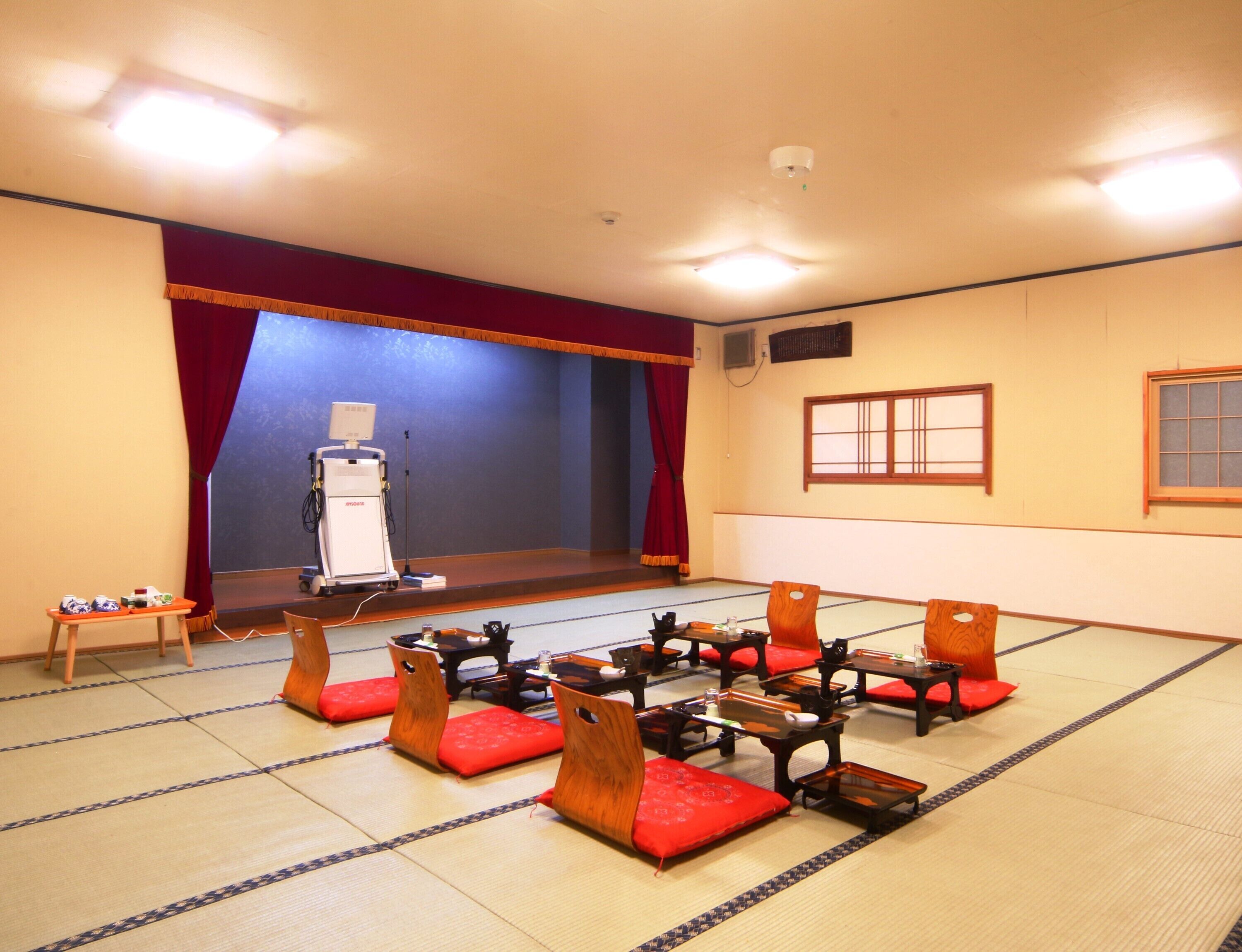 Um quarto japonês tradicional com chão de tatame, mobiliário de madeira e um palco com projetor.