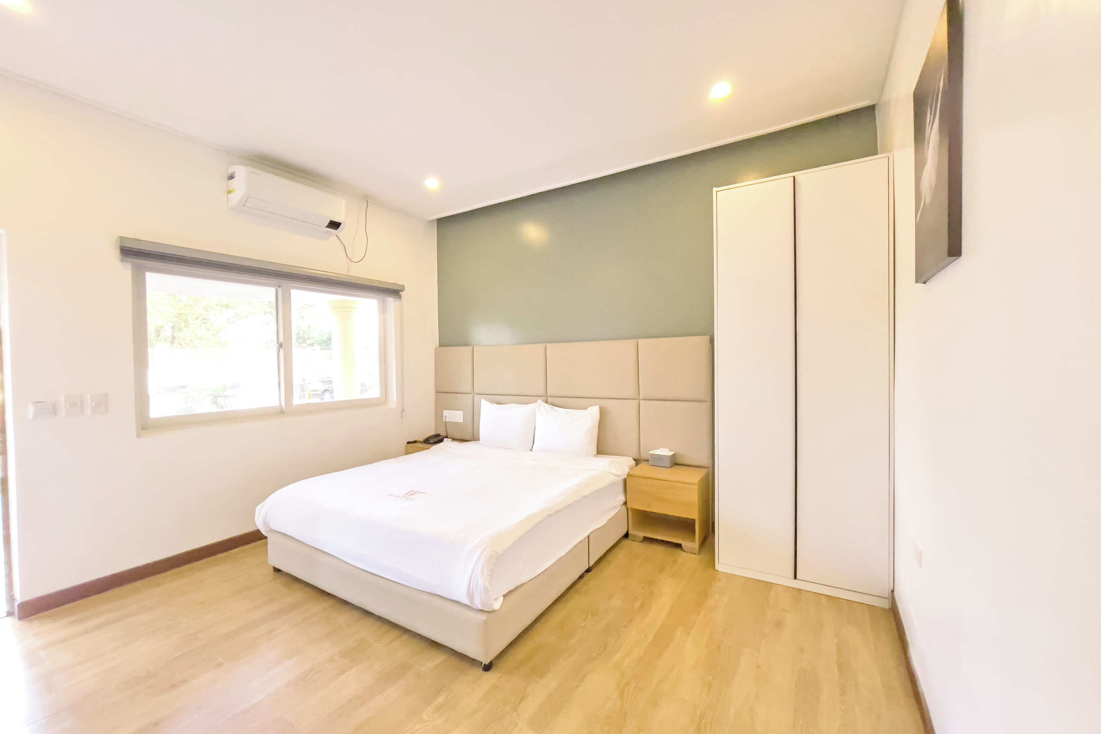 Quarto moderno com cama grande, mesas de cabeceira, guarda-roupa e uma janela.