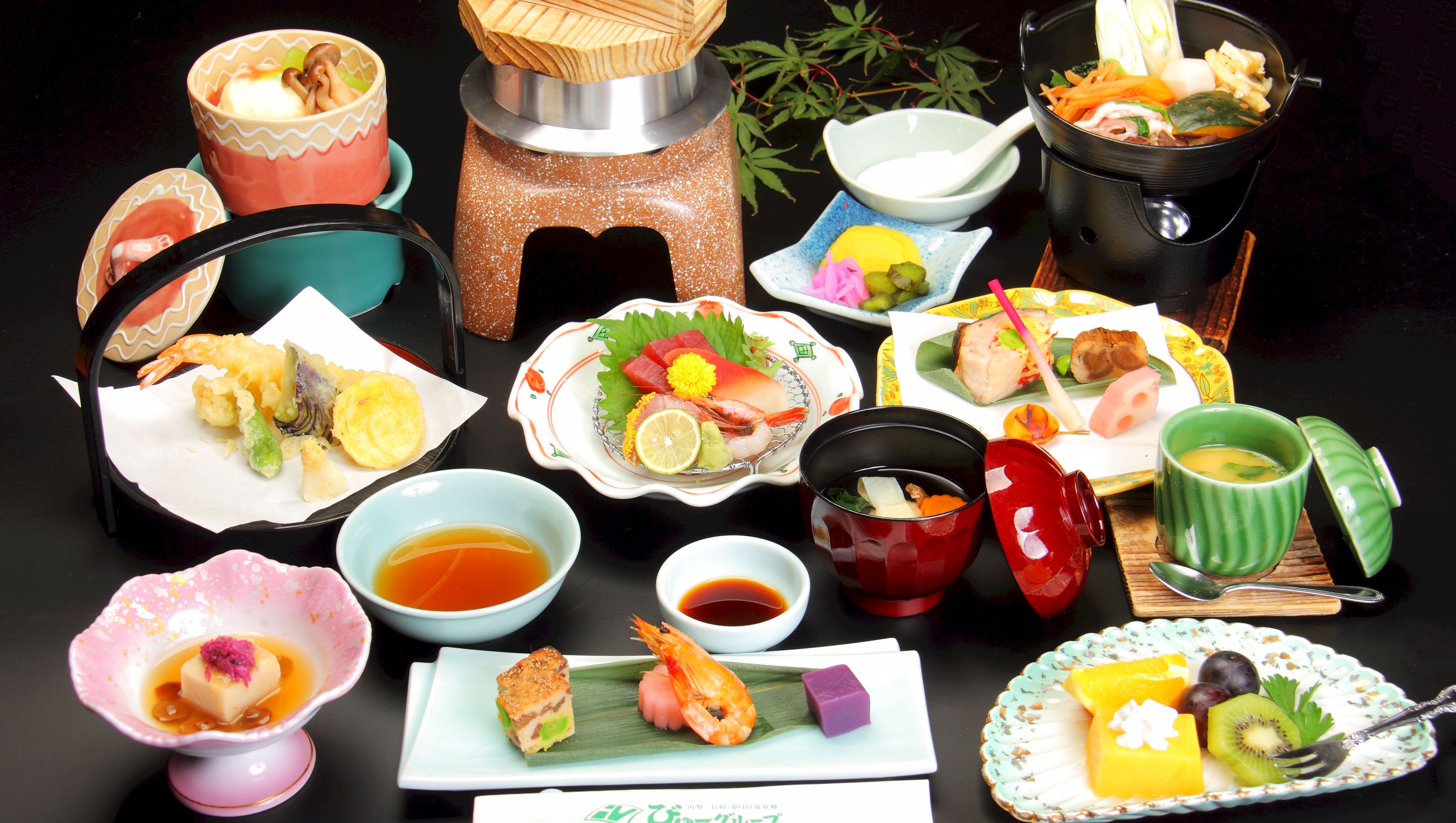 Diversos pratos japoneses, incluindo sushi, sashimi e tempura, servidos sobre uma mesa preta com várias tigelas e pratos.